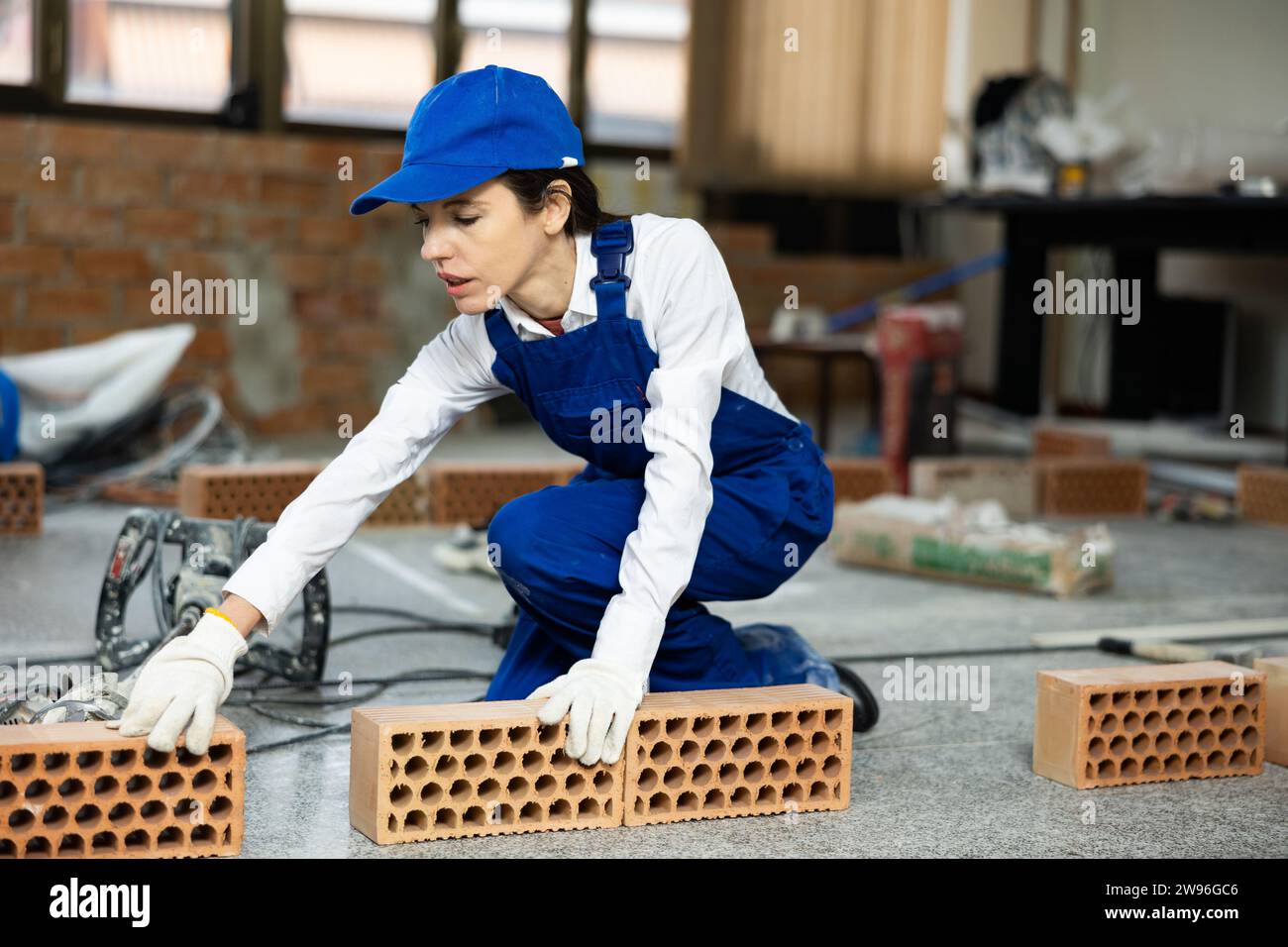 Female builder in blue workwear planning erection of partition wall in ...