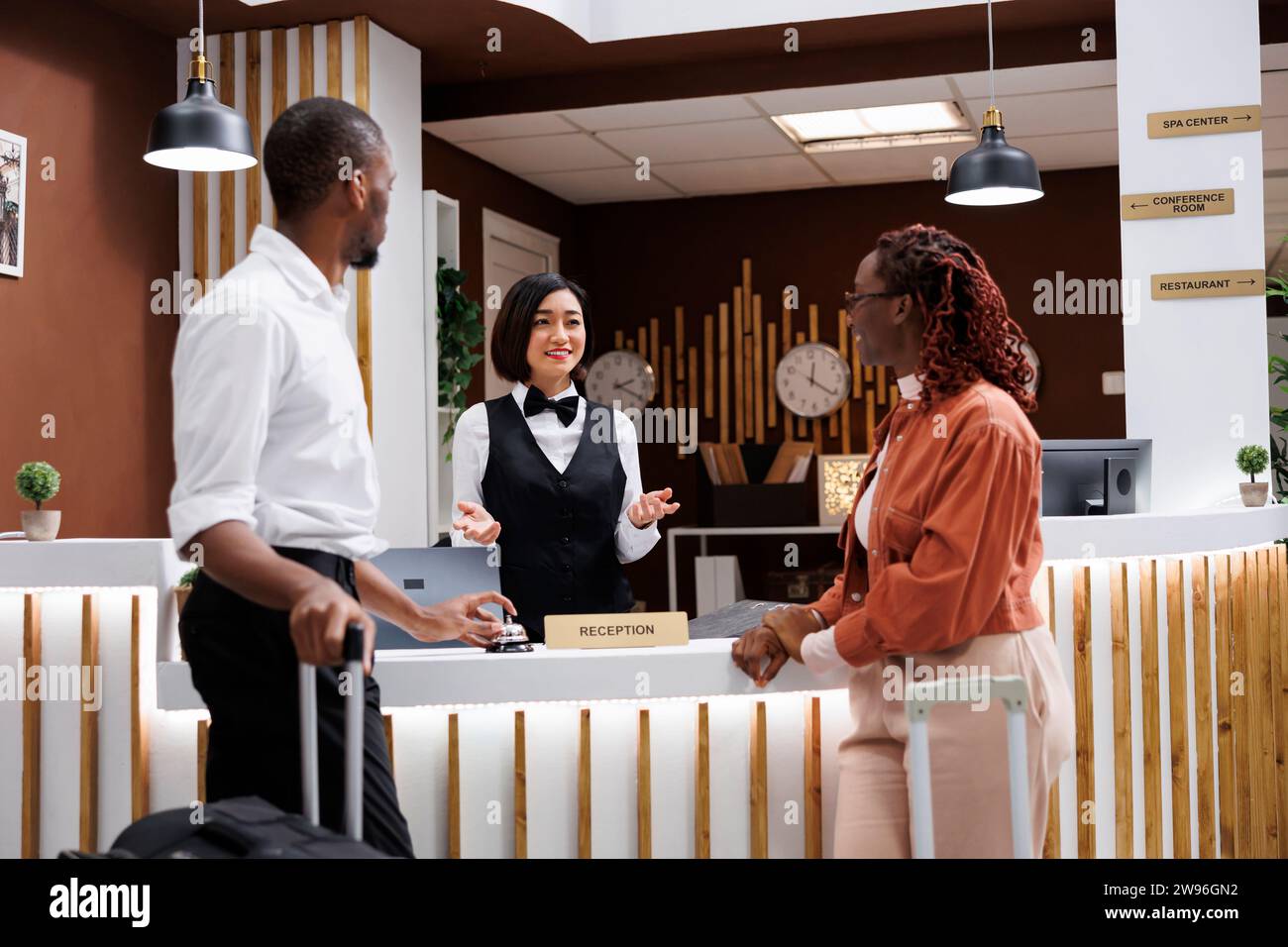 Asian woman helping guests to check in at reception desk, using records ...