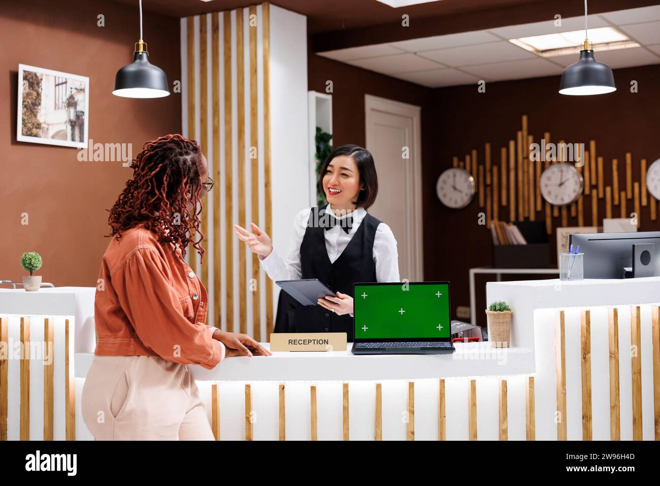 Diverse women using greenscreen display at hotel front desk, talking ...