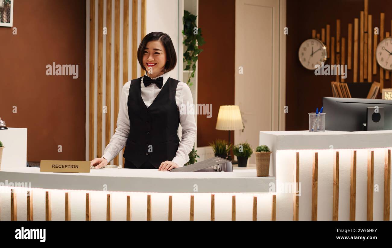 Smiling professional hotel employee taking phone calls while working at ...