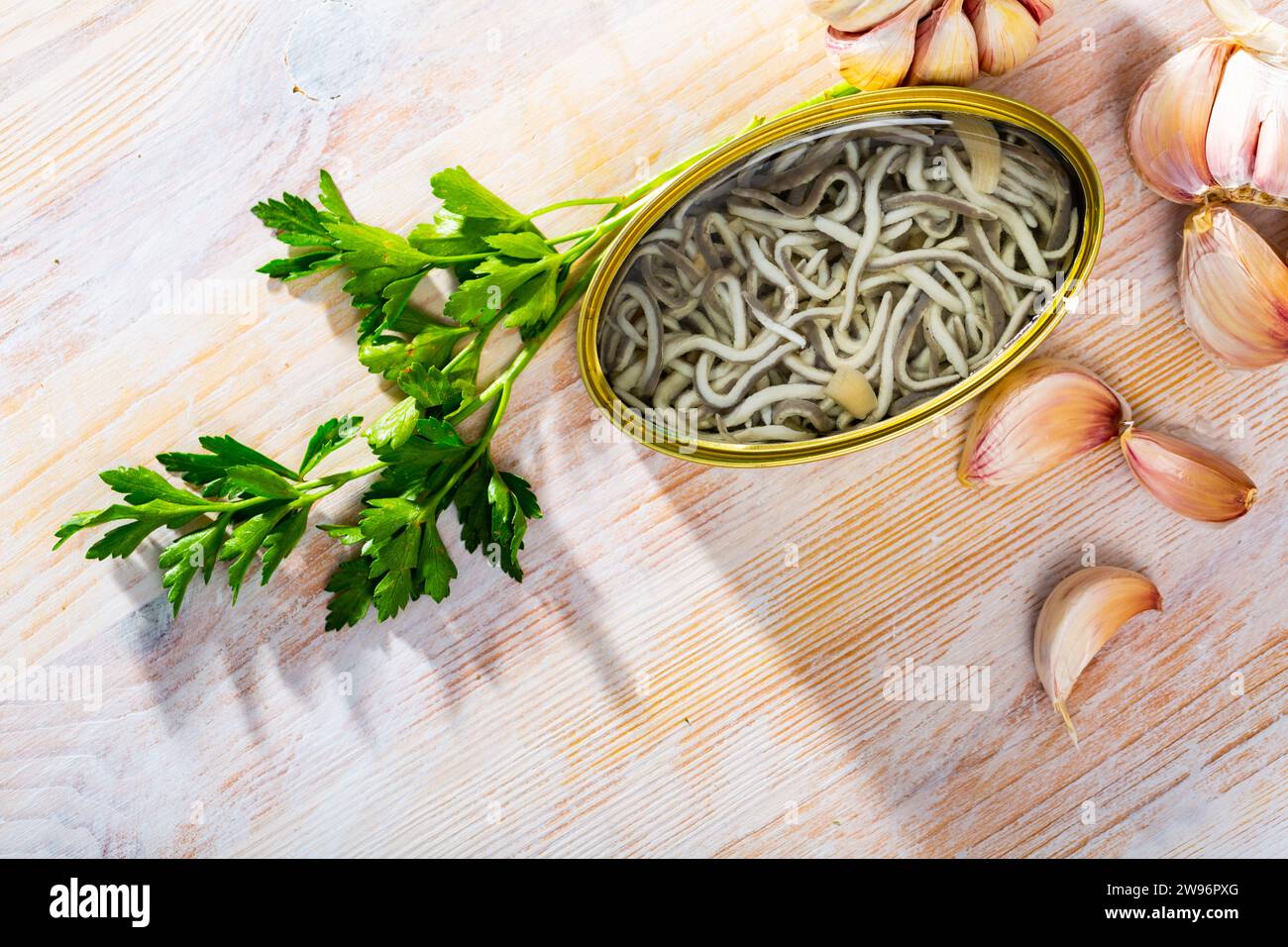 Image of pickled eels in open tin can with garlic at table, nobody ...