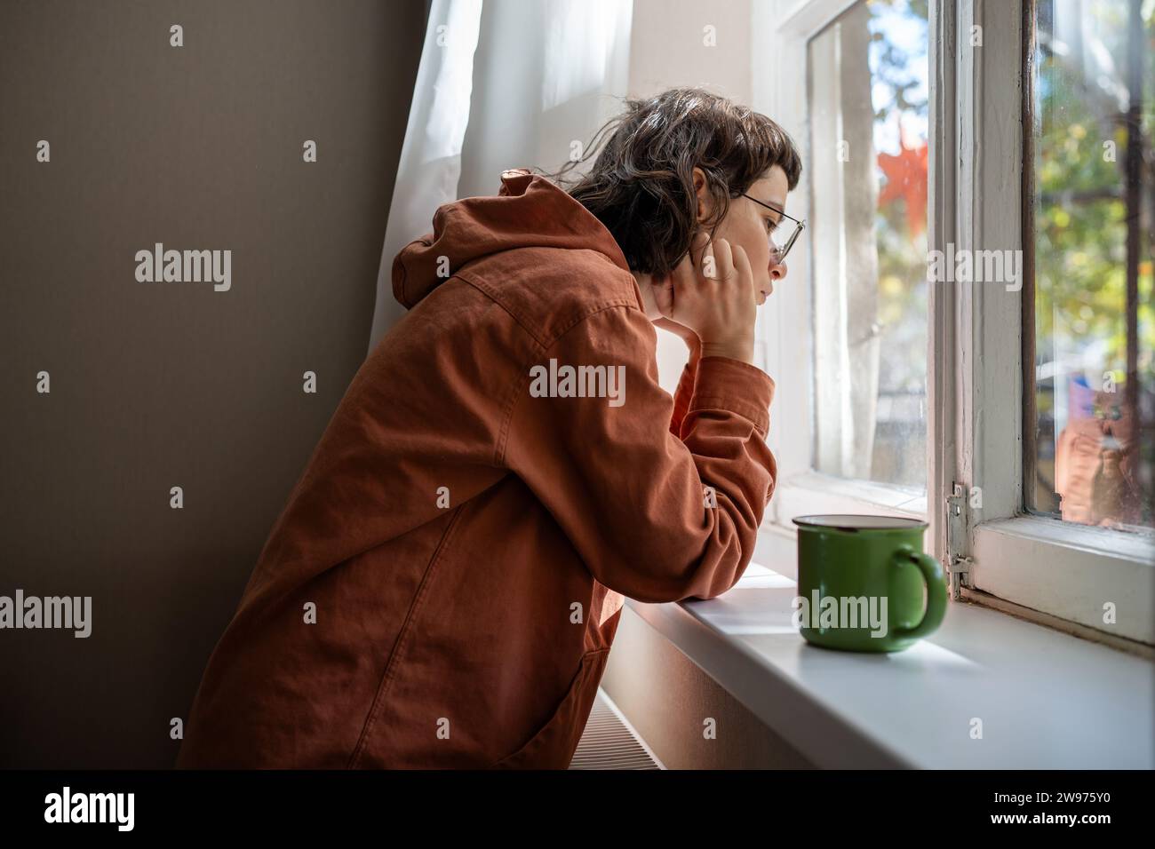 Introverted teen girl standing near window, looking at street ...