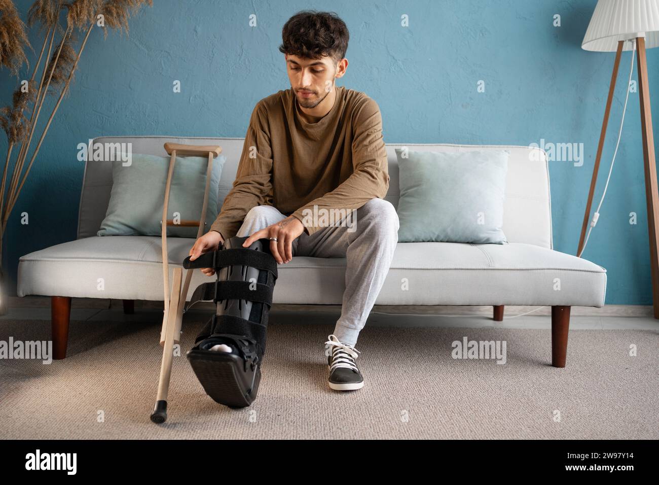 A young man with an ankle injury wearing a rigid ankle orthosis sits on ...