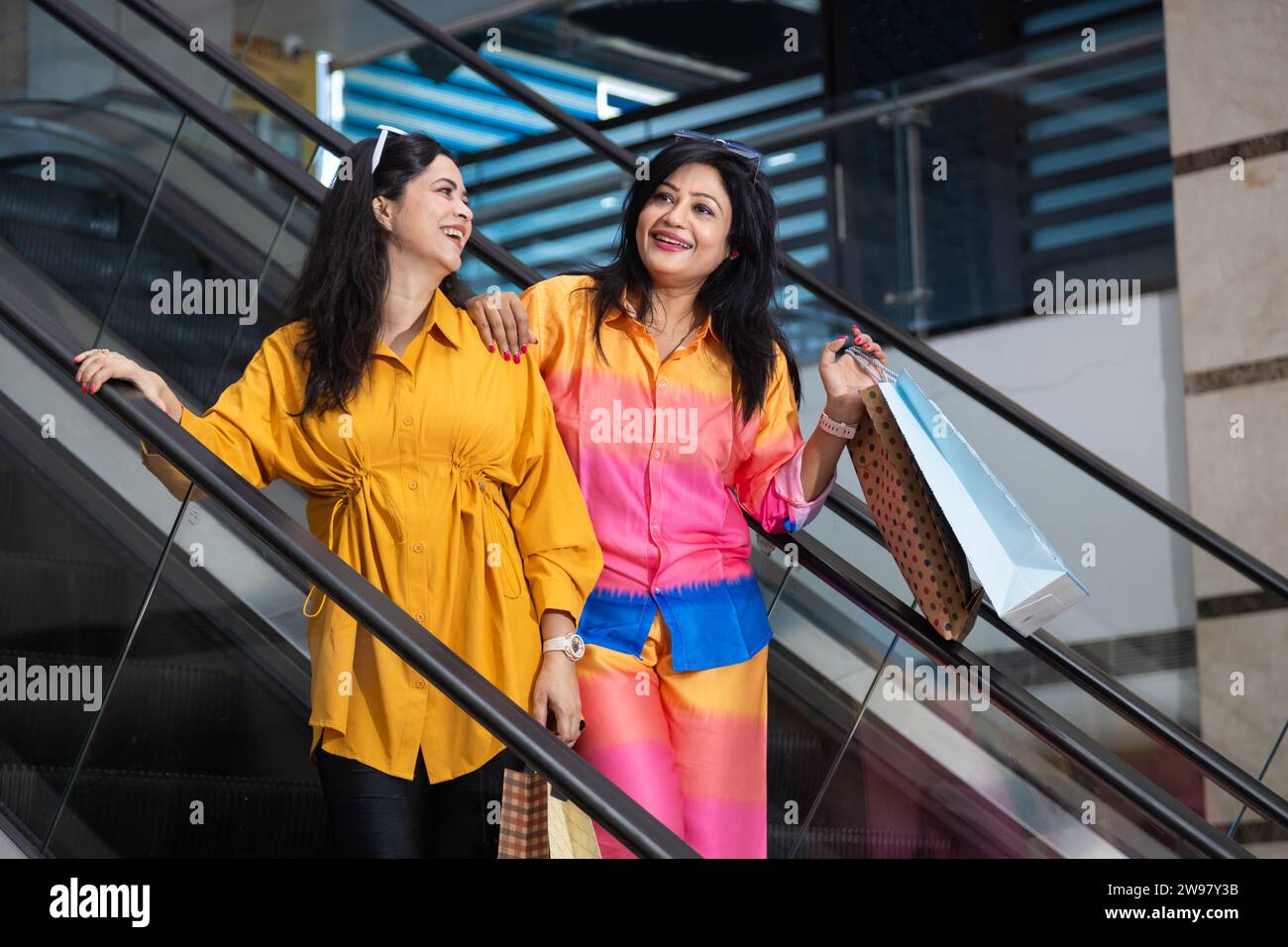 Two Happy indian women holding on escalator handrail and riding ...