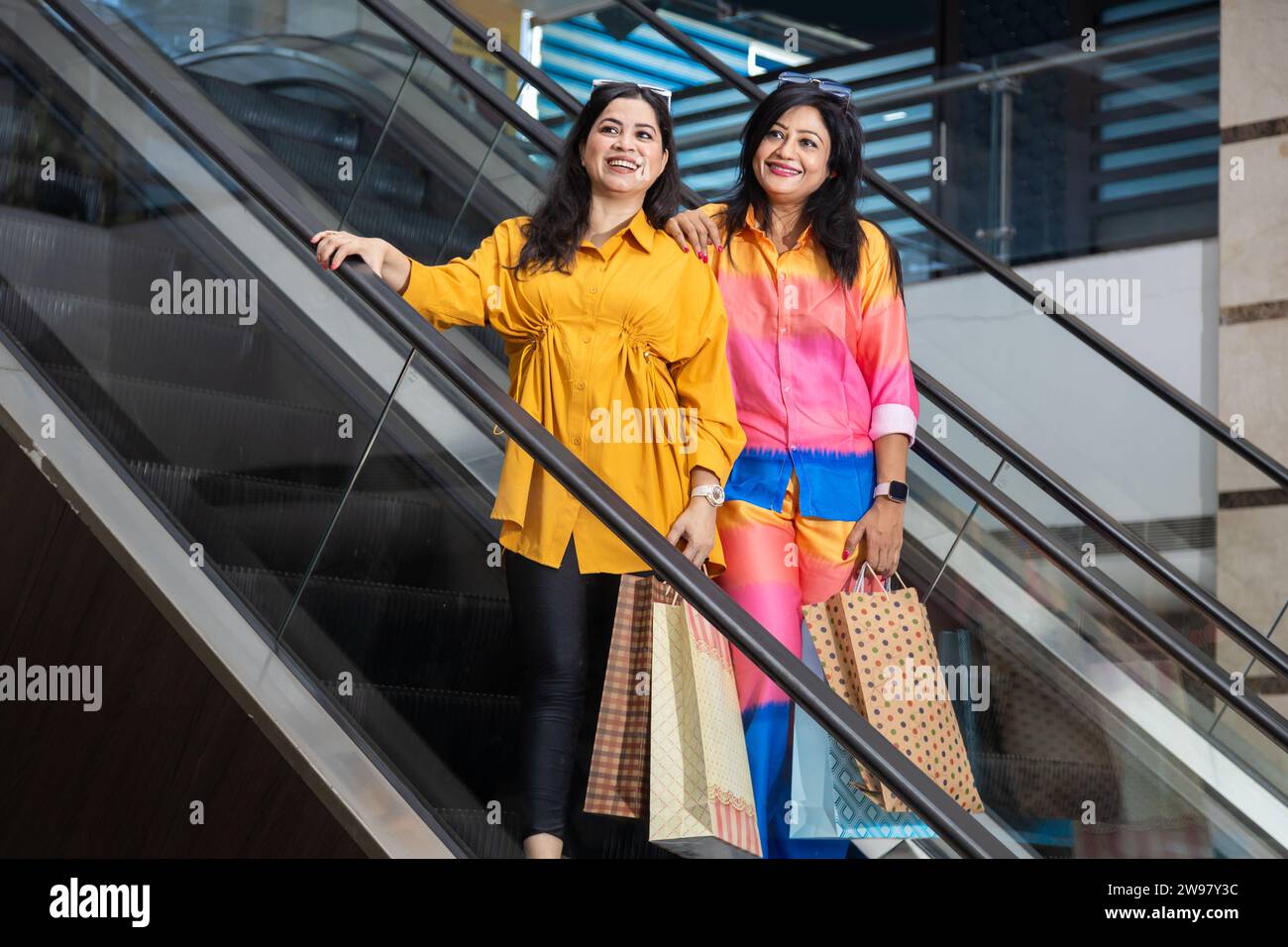 Two Happy indian women holding on escalator handrail and riding ...