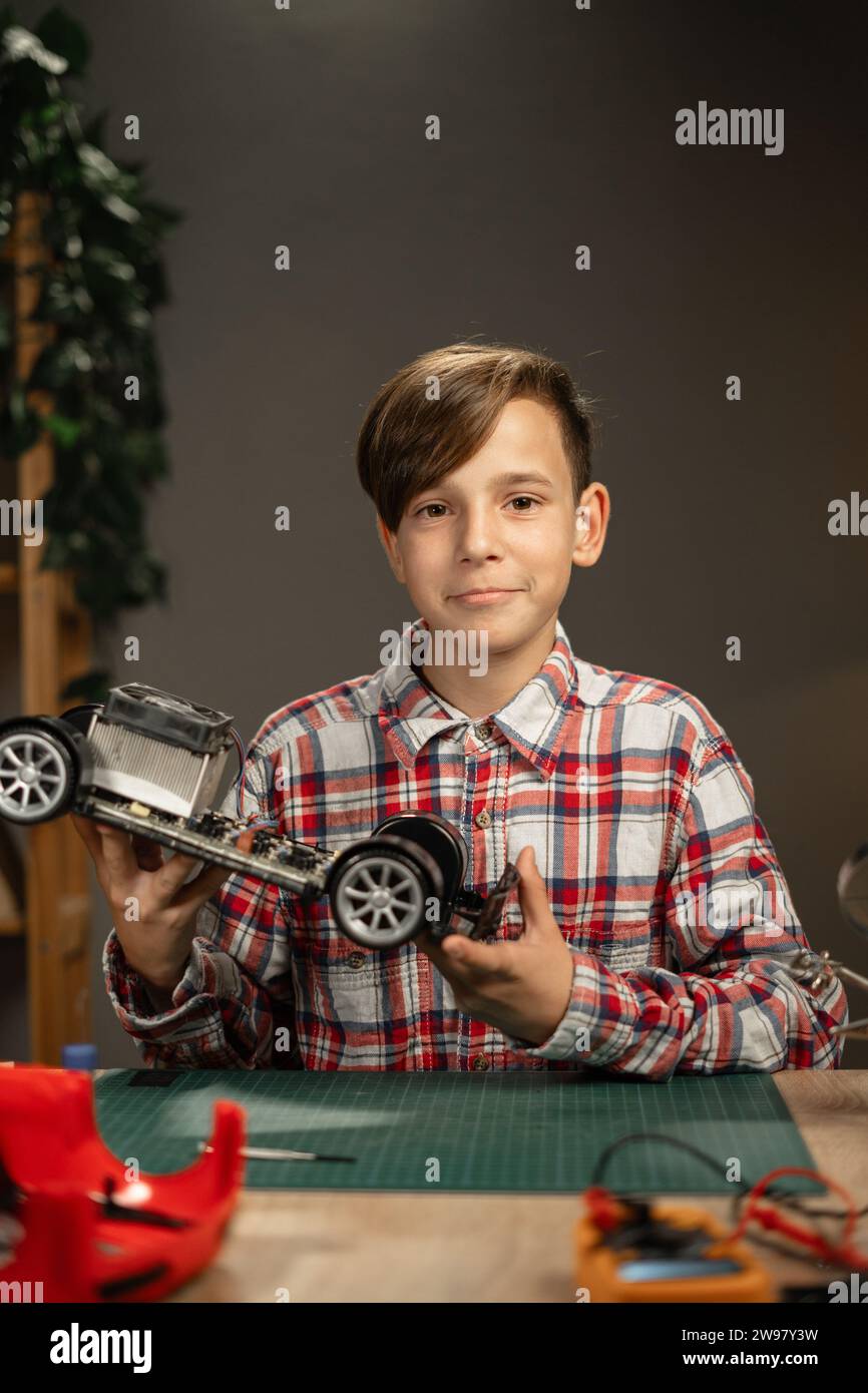 Portrait of a boy repairing a toy car with soldering wires looking at ...