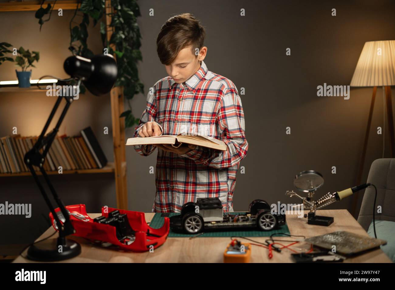 Caucasian boy with old book soldering broken remote controlled car at ...