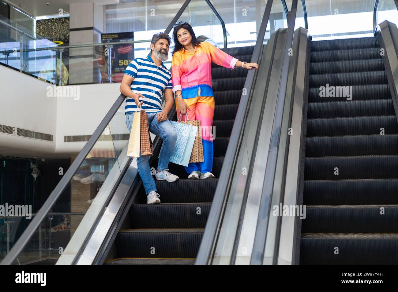 Happy indian couple holding on escalator handrail and riding escalator ...