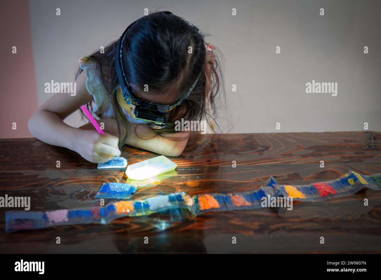 Pasting gemstones, a little girl is making artwork with her own hands ...