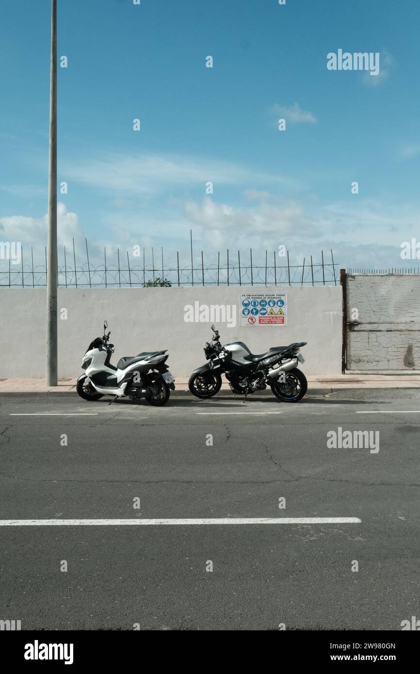 Two motorcycles parked up against a concrete wall by the side of the ...