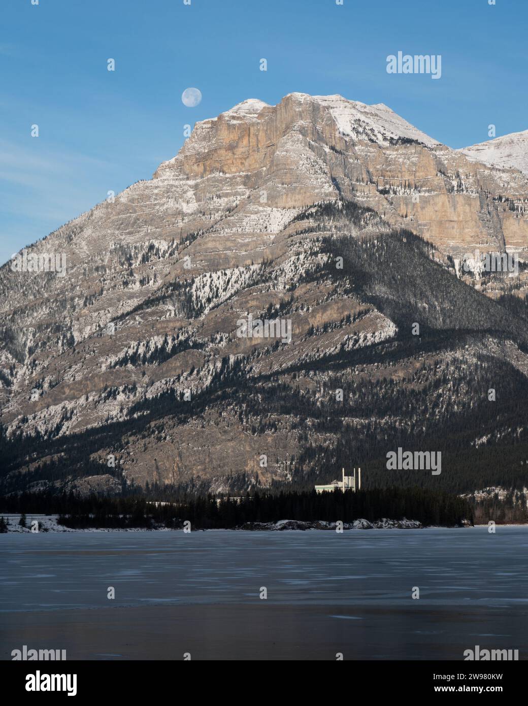 A spectacular scene of a full moon setting behind a mountain range in Lac Des Arcs, Alberta ...