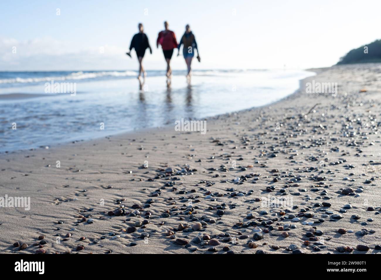 Three people of different ages walking along a pristine sandy beach ...