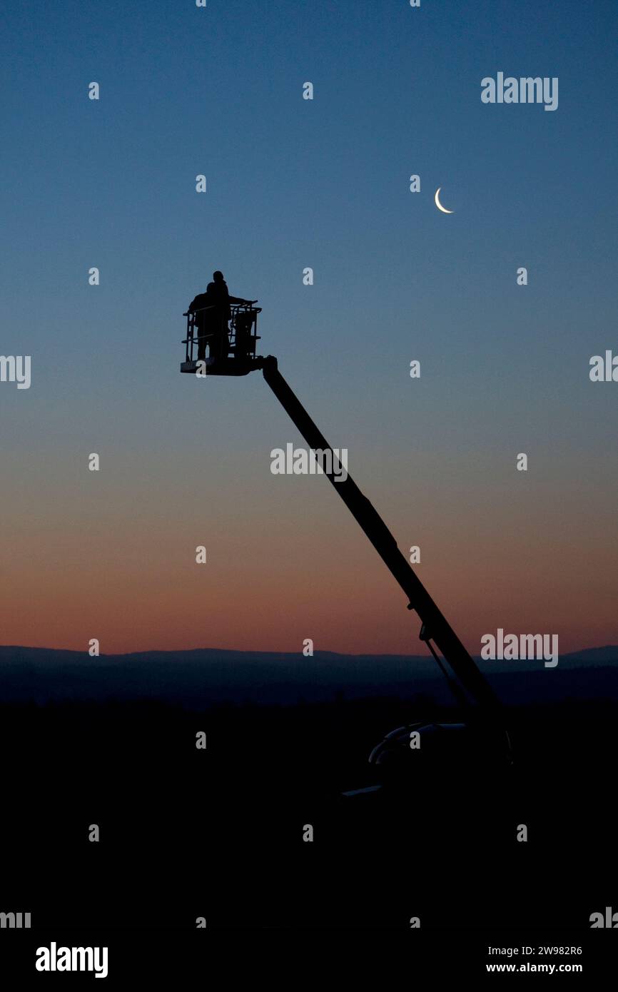 Two men aloft in a crane as a crescent moon rises Stock Photo - Alamy