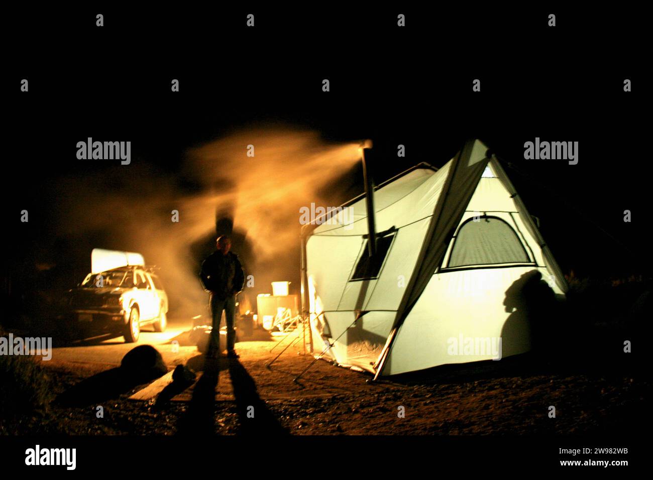 A man stands silhouetted against smoke emanating from a tent's furnace ...