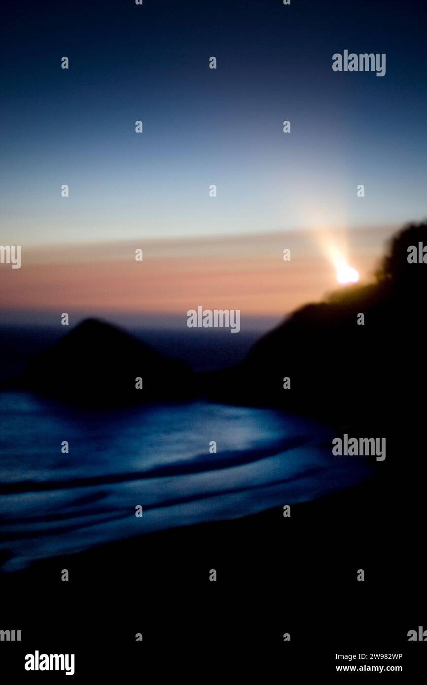 A lighthouse's light is bright over a bay at dusk. (Blurred Image Stock ...