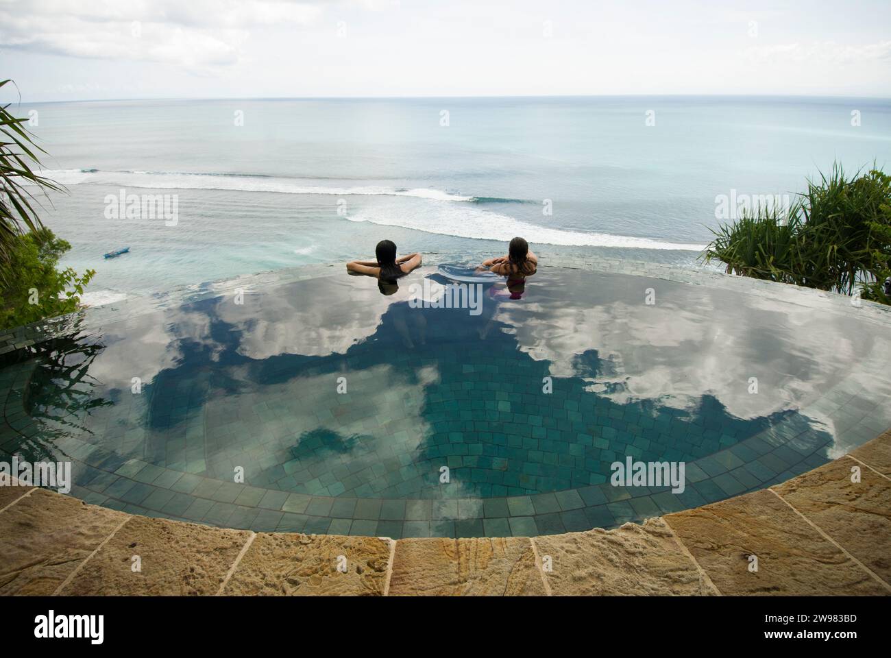 Two women peer out over the ocean from the edge of an infinity pool ...