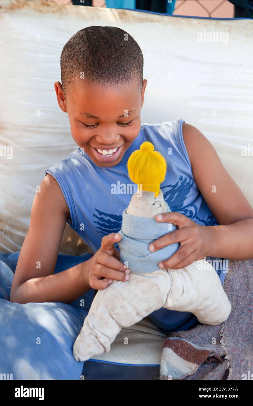 african child in the village, playing with a cloth doll outdoors in the ...