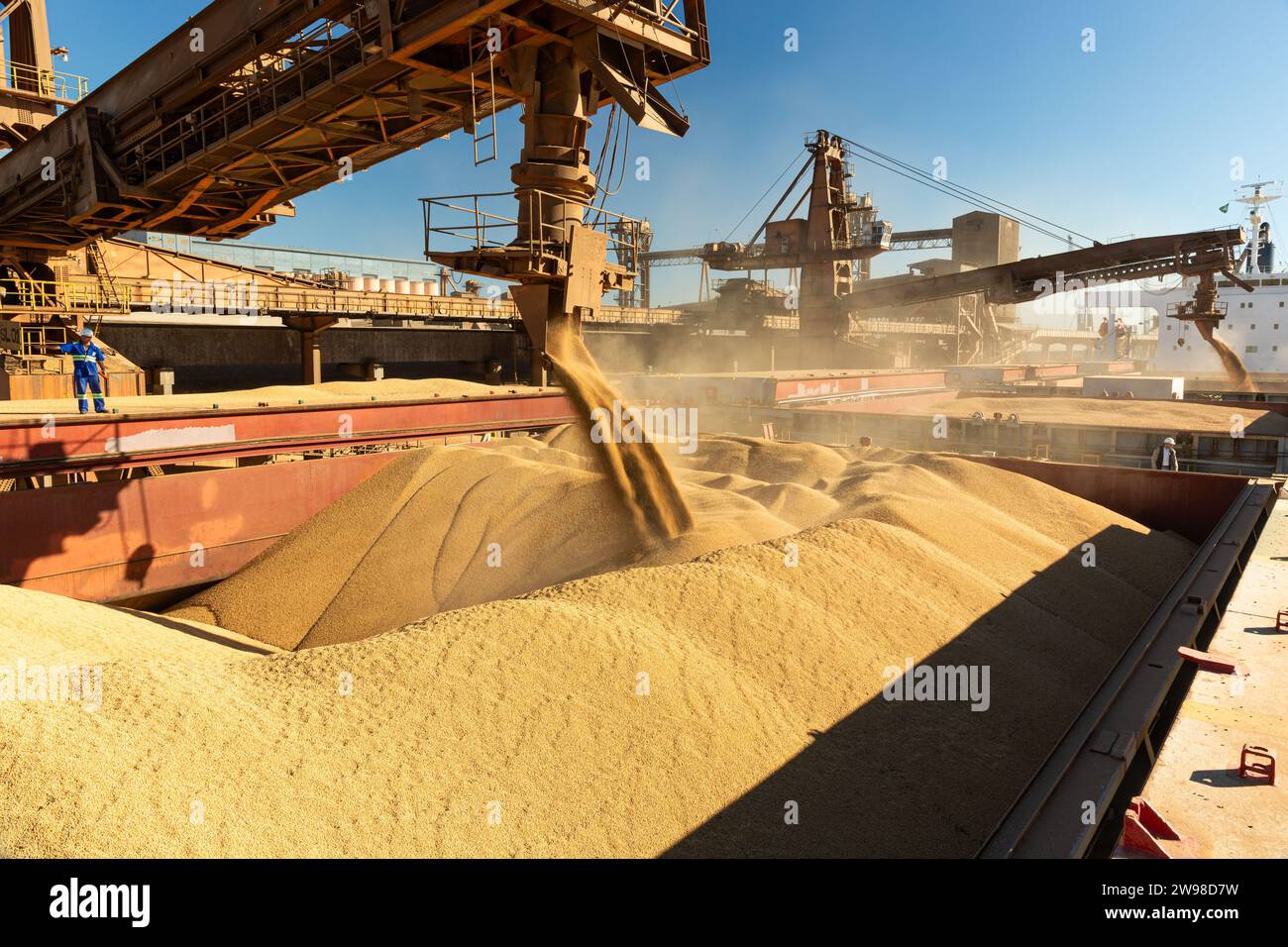 in a port we see two cranes loading soybeans onto a cargo ship, with ...