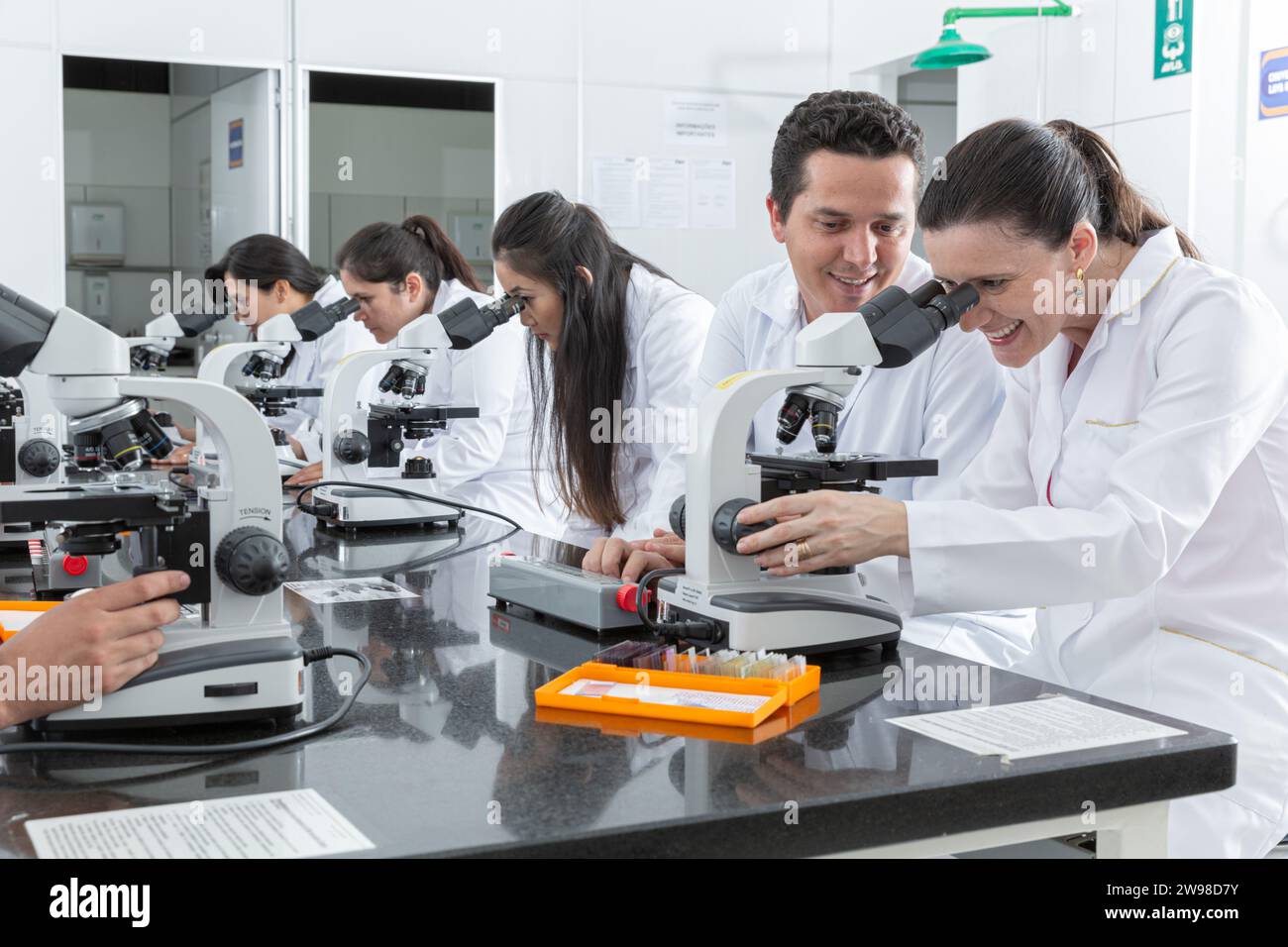 Scientists examining microscope, in laboratory room, with partner ...