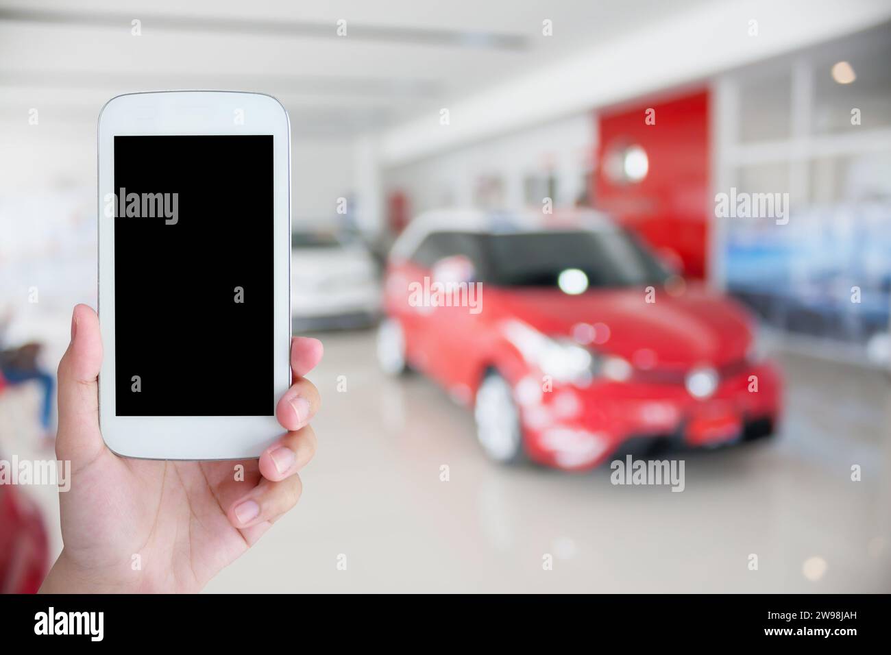 hand holding mobile phone with blurred background of new cars in ...