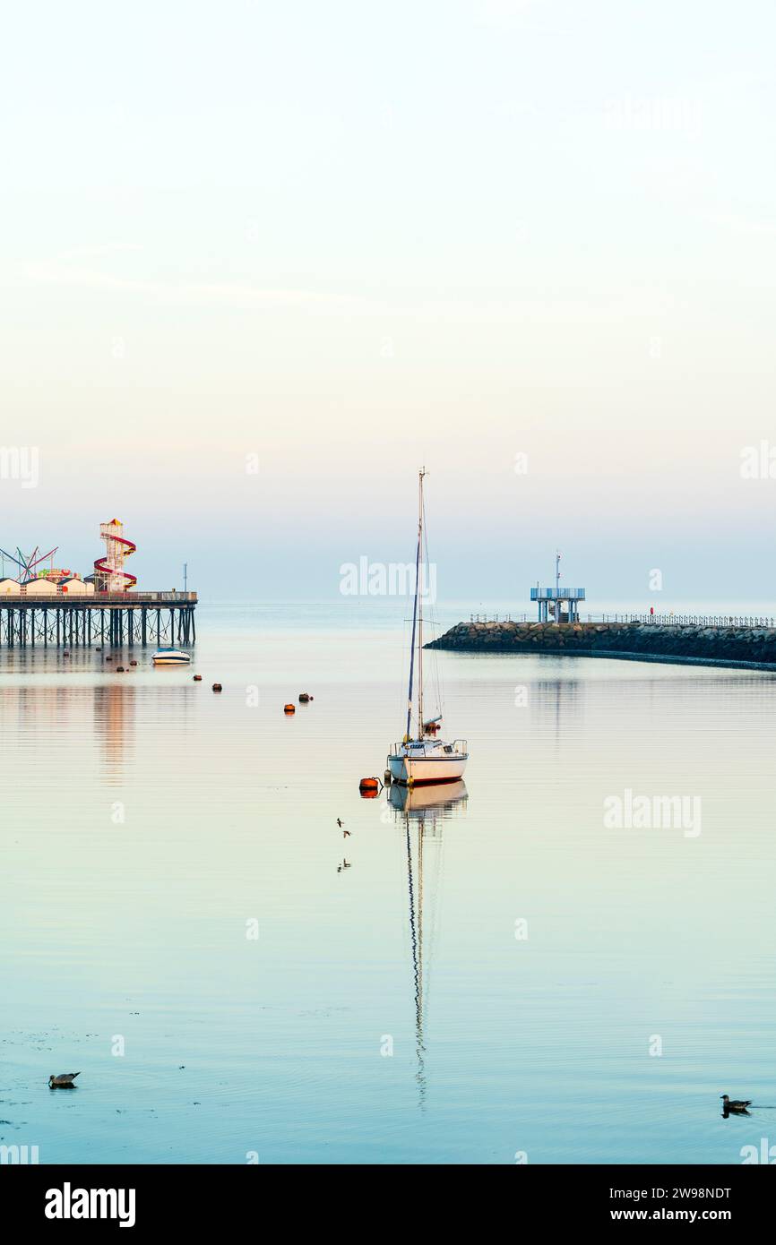 Herne Bay harbour in a pastel coloured dawn. Very still water, a single ...