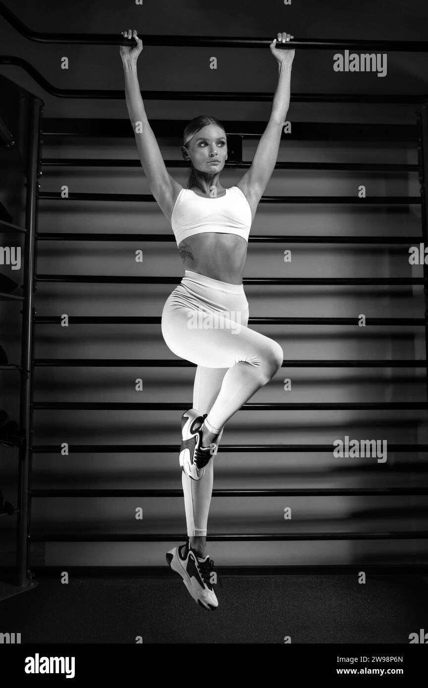 Beautiful tall blonde pulls up on the bar in the gym against the ...