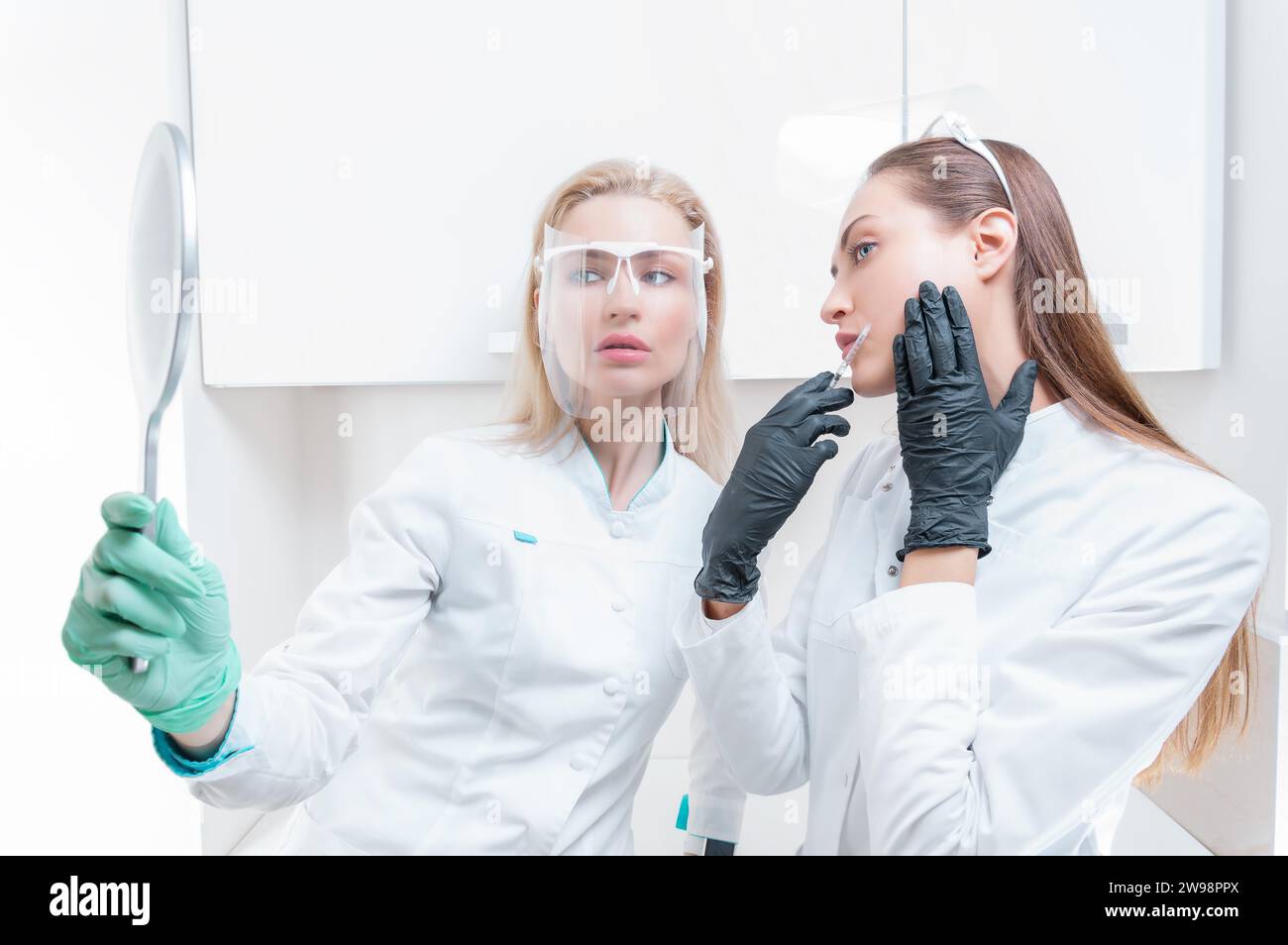 Two beauticians pose in a medical salon with a mirror in their hands ...