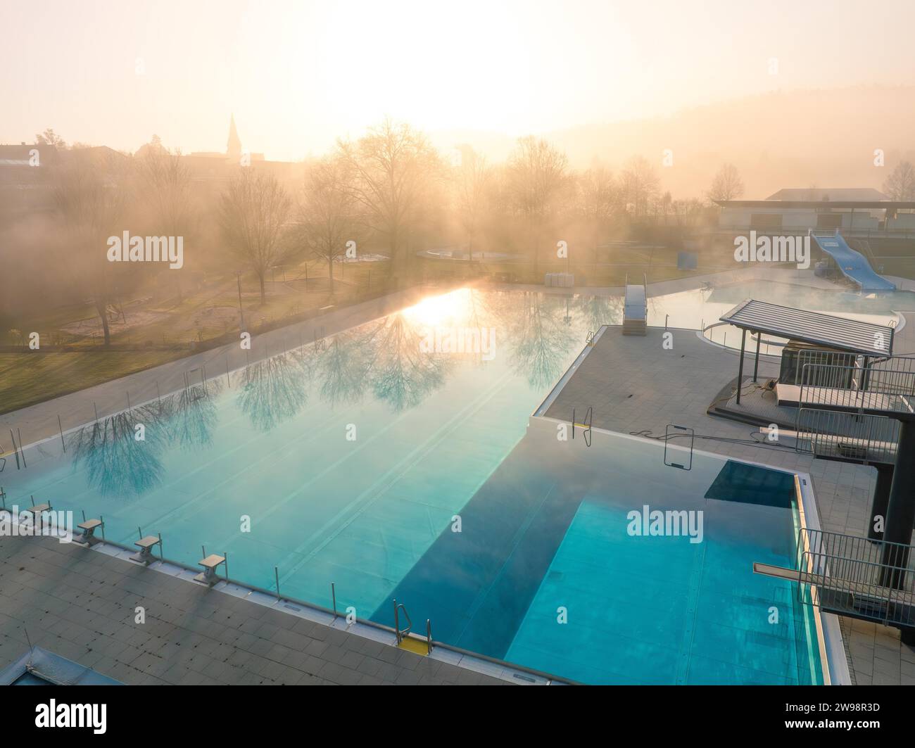 Morning light reflected in the water of a fog-covered swimming pool ...