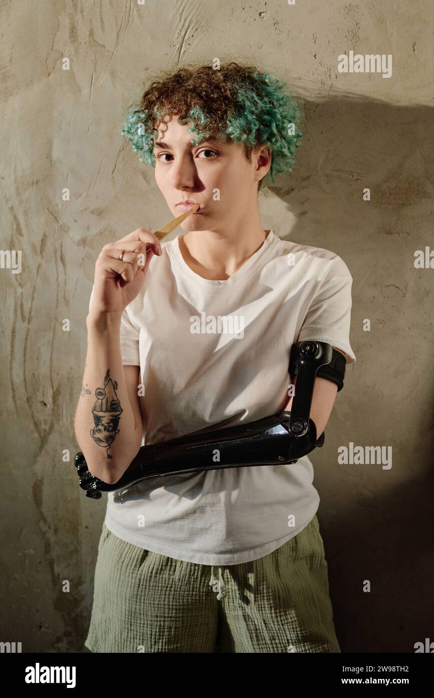 Portrait of young woman with prosthetic arm brushing teeth in morning ...