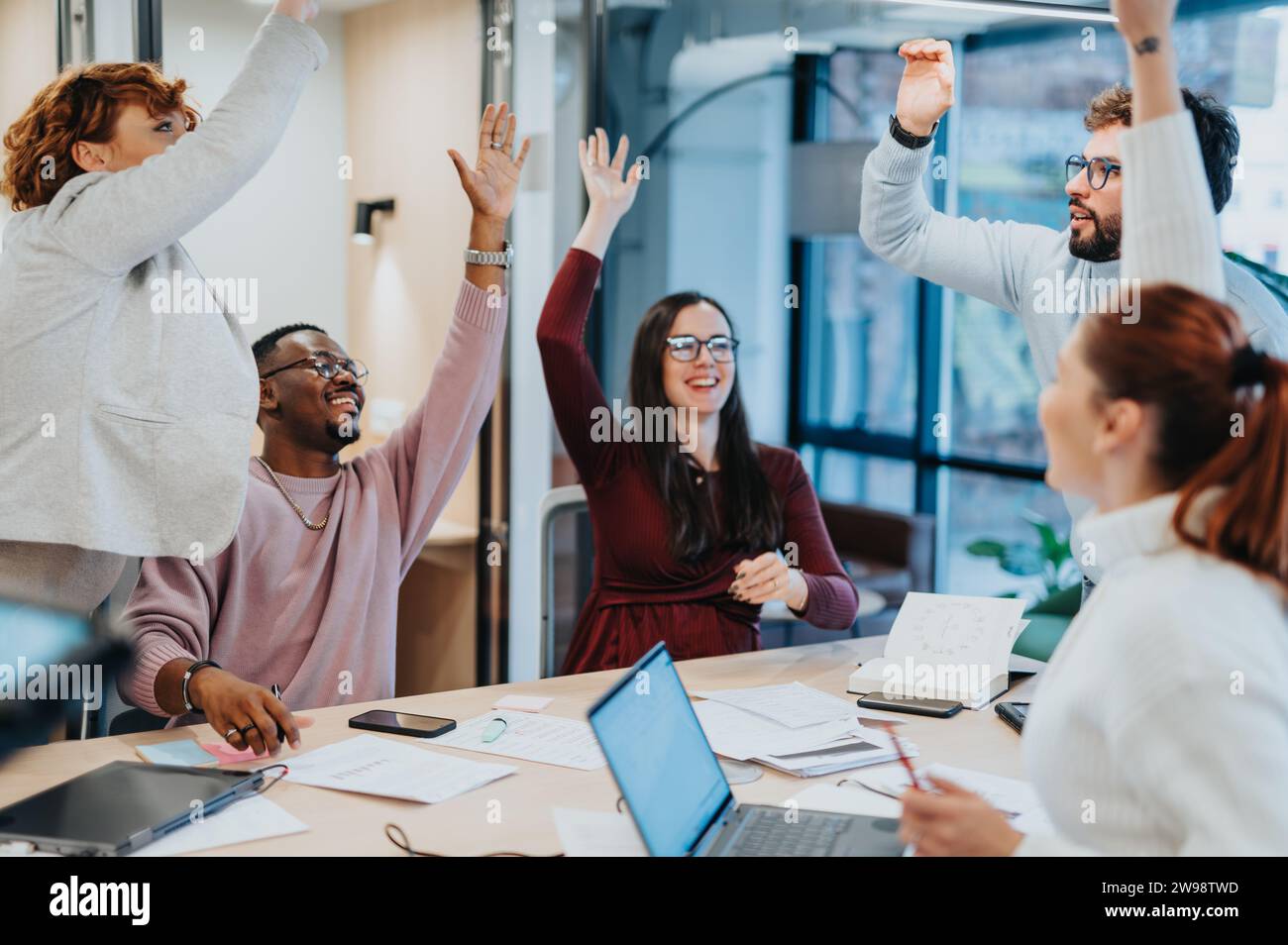 Multiethnic colleagues celebrate a success. Smiling and raising arms, they showcase teamwork ...