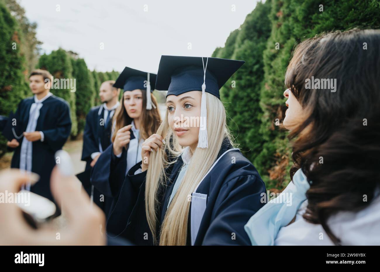 Graduates celebrating achievement. Smiling in gowns and caps, they take ...