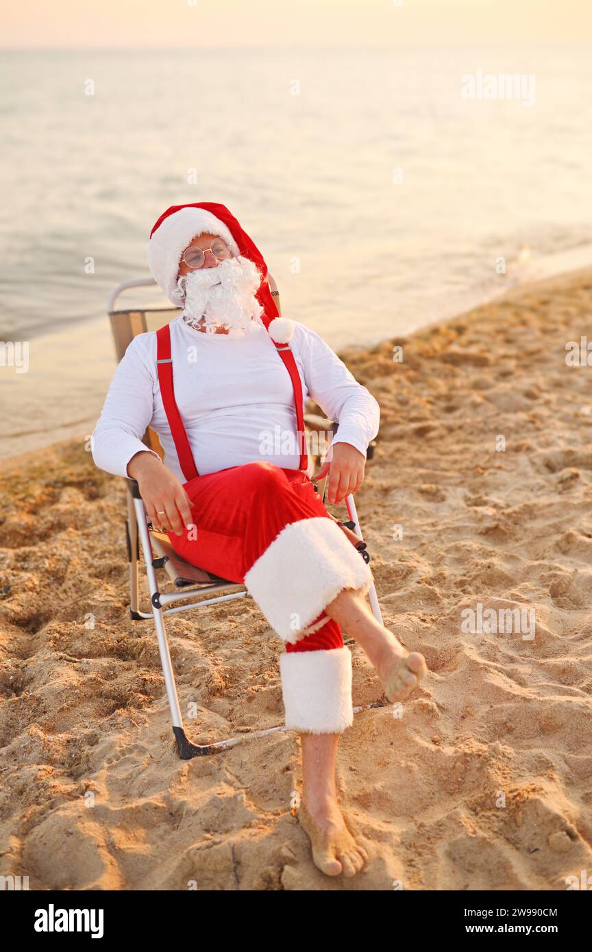 Santa barefoot in red suspenders sitting on a chaise lounge resting ...