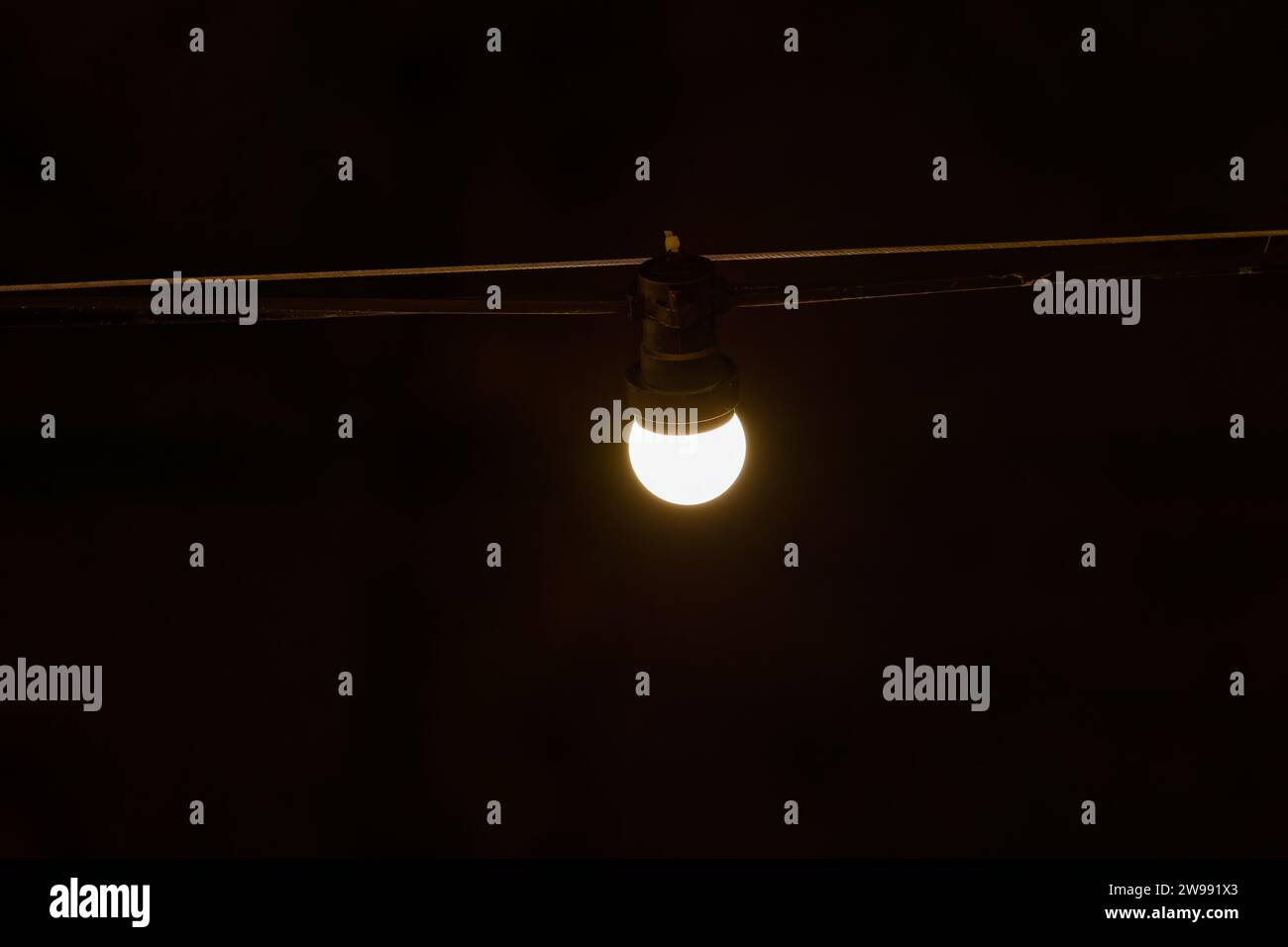 An outdoor light suspended from an electrical wire in a night setting ...