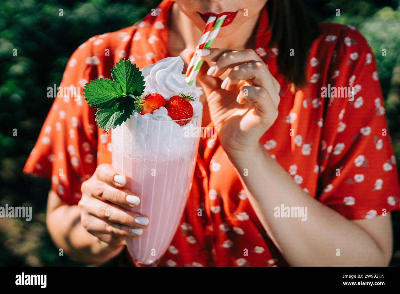 Pretty woman drinking strawberry milkshake cocktail with straw, nature ...