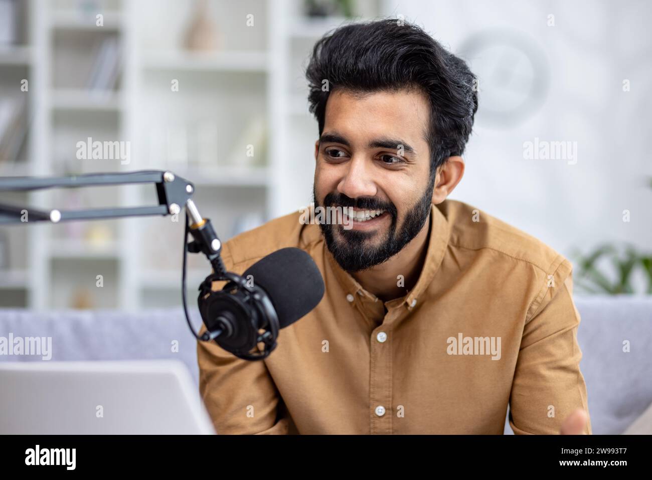 Close-up photo of a young Indian man smiling sitting on the couch at ...