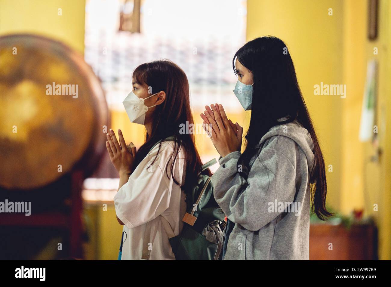 The young female Buddhist worshipers in masks praying at the altars of ...