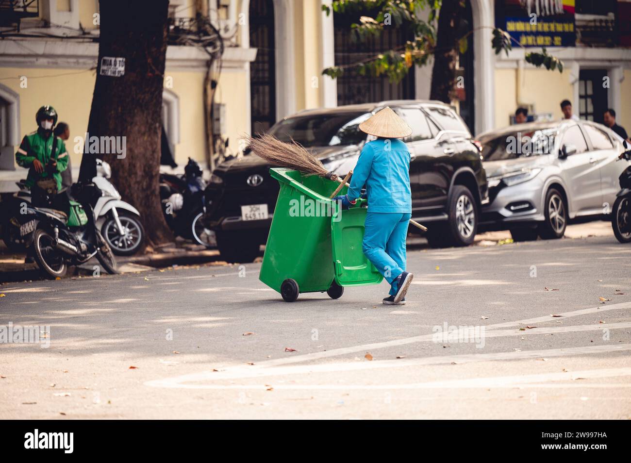 A street sweeper with blue clothing and a salakot hat carrying the ...