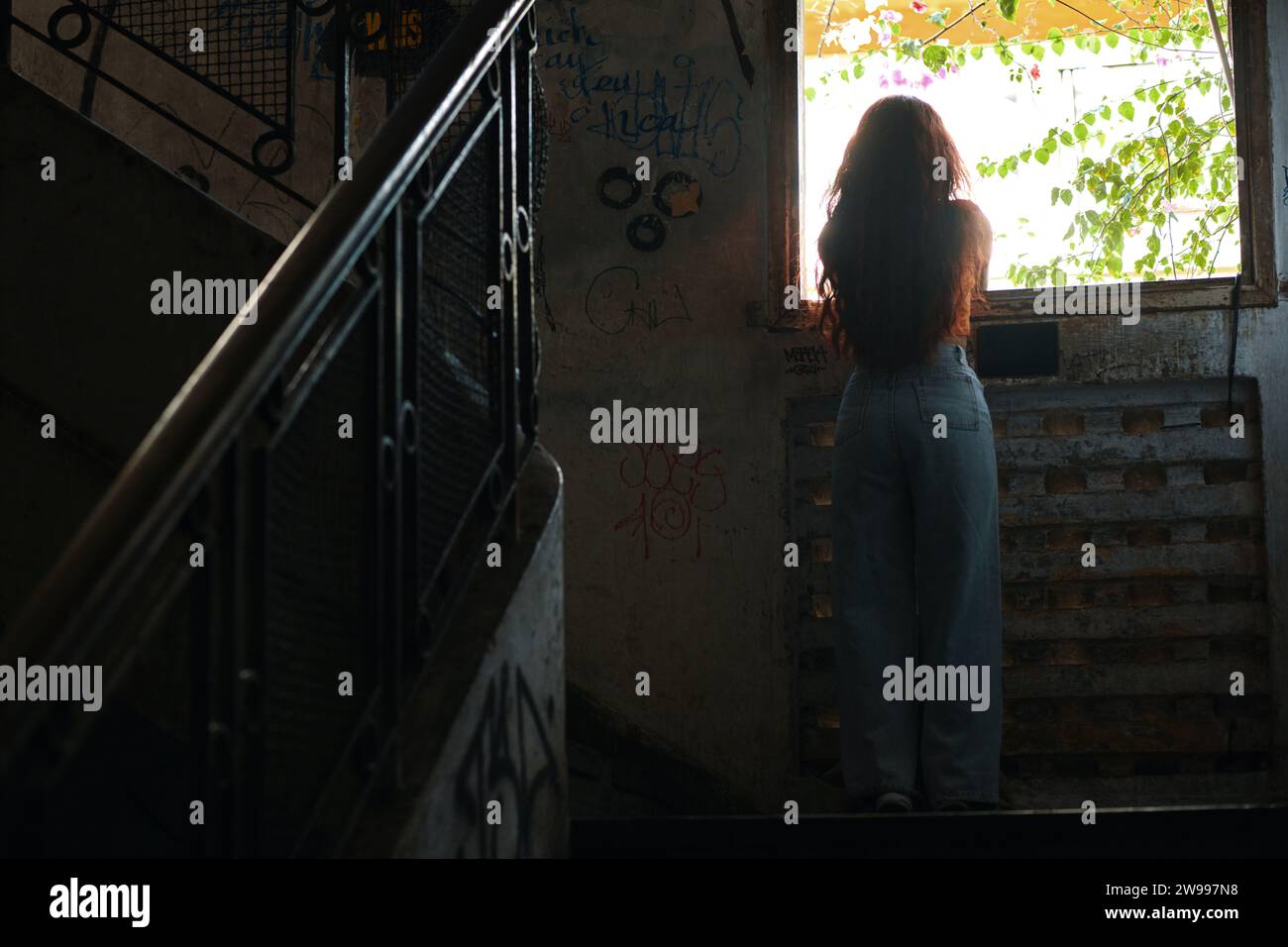 Young woman with long hair looking though window of abandoned and ...