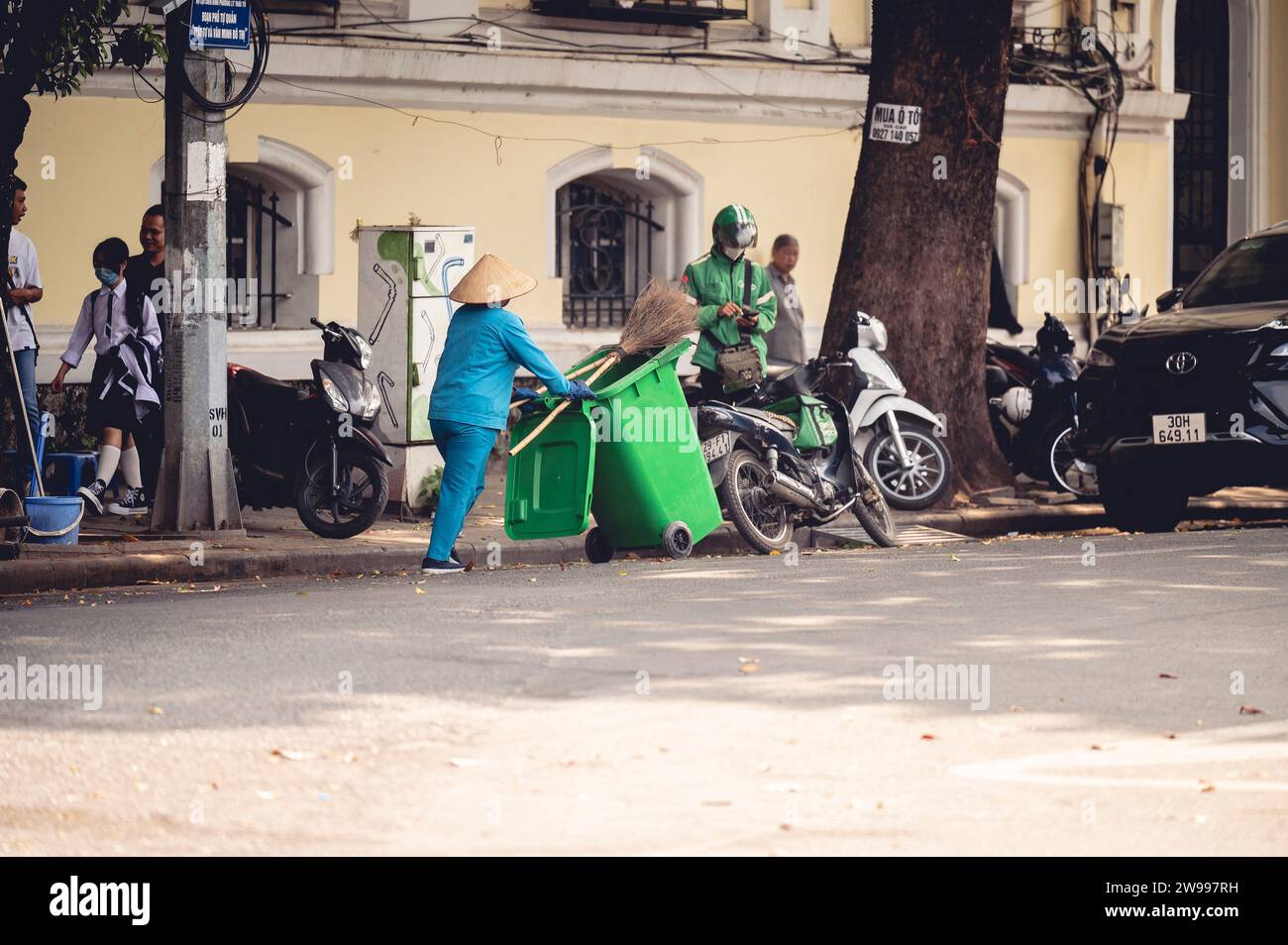 A street sweeper with blue clothing and a salakot hat carrying the ...