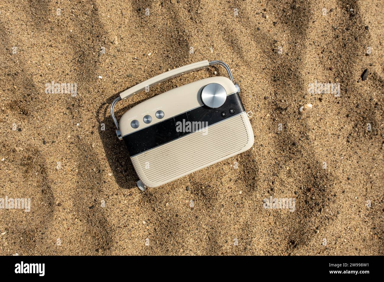 A classic radio set on a sandy beach surrounded by rocks, with a ...
