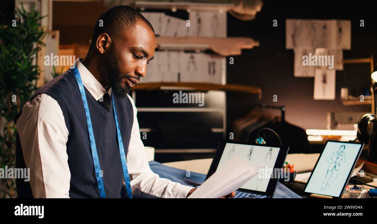 African american tailor checking sketches, using laptop and outlines on ...