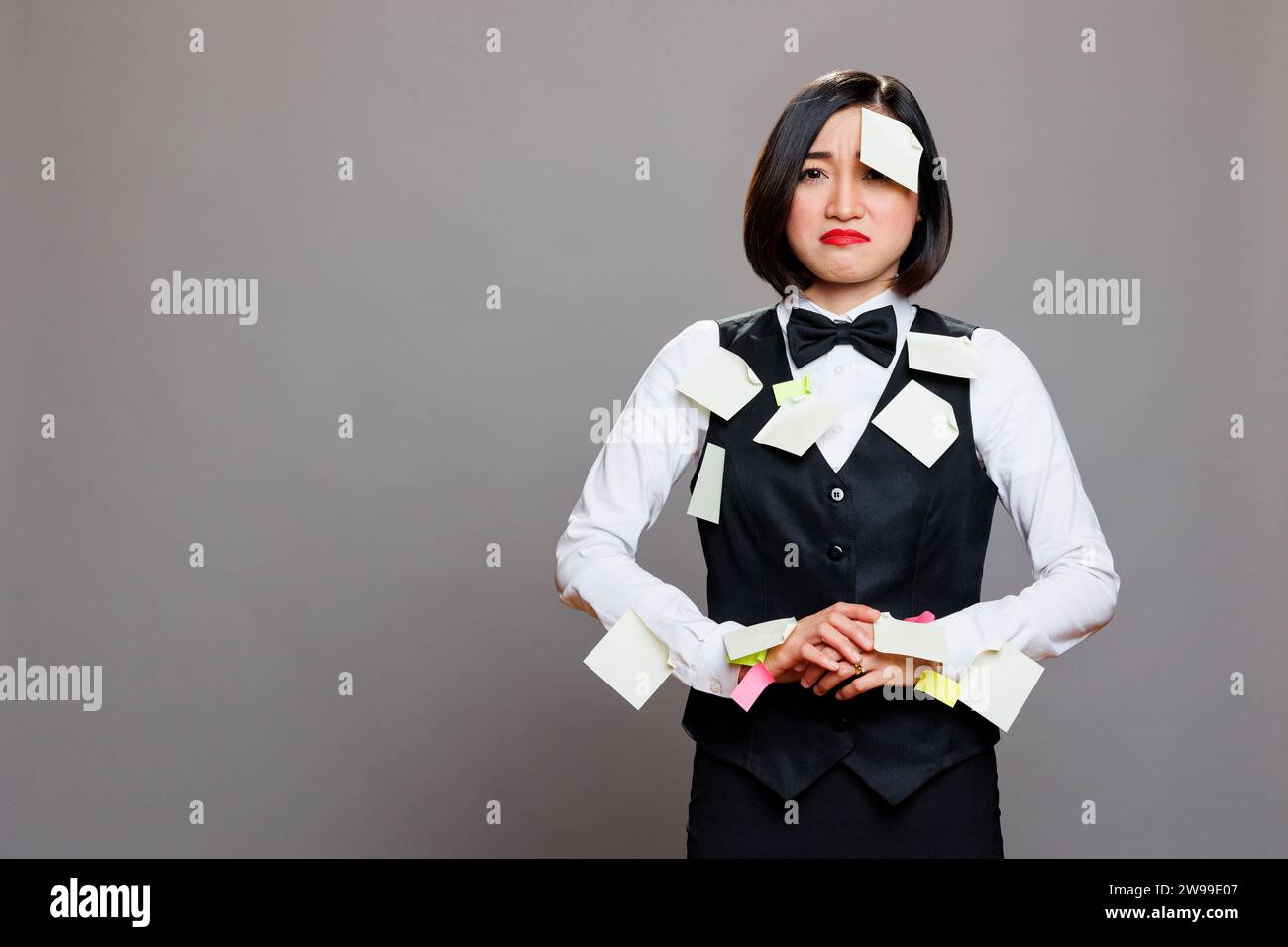 Unhappy exhausted asian waitress covered with tasks sticky notes ...