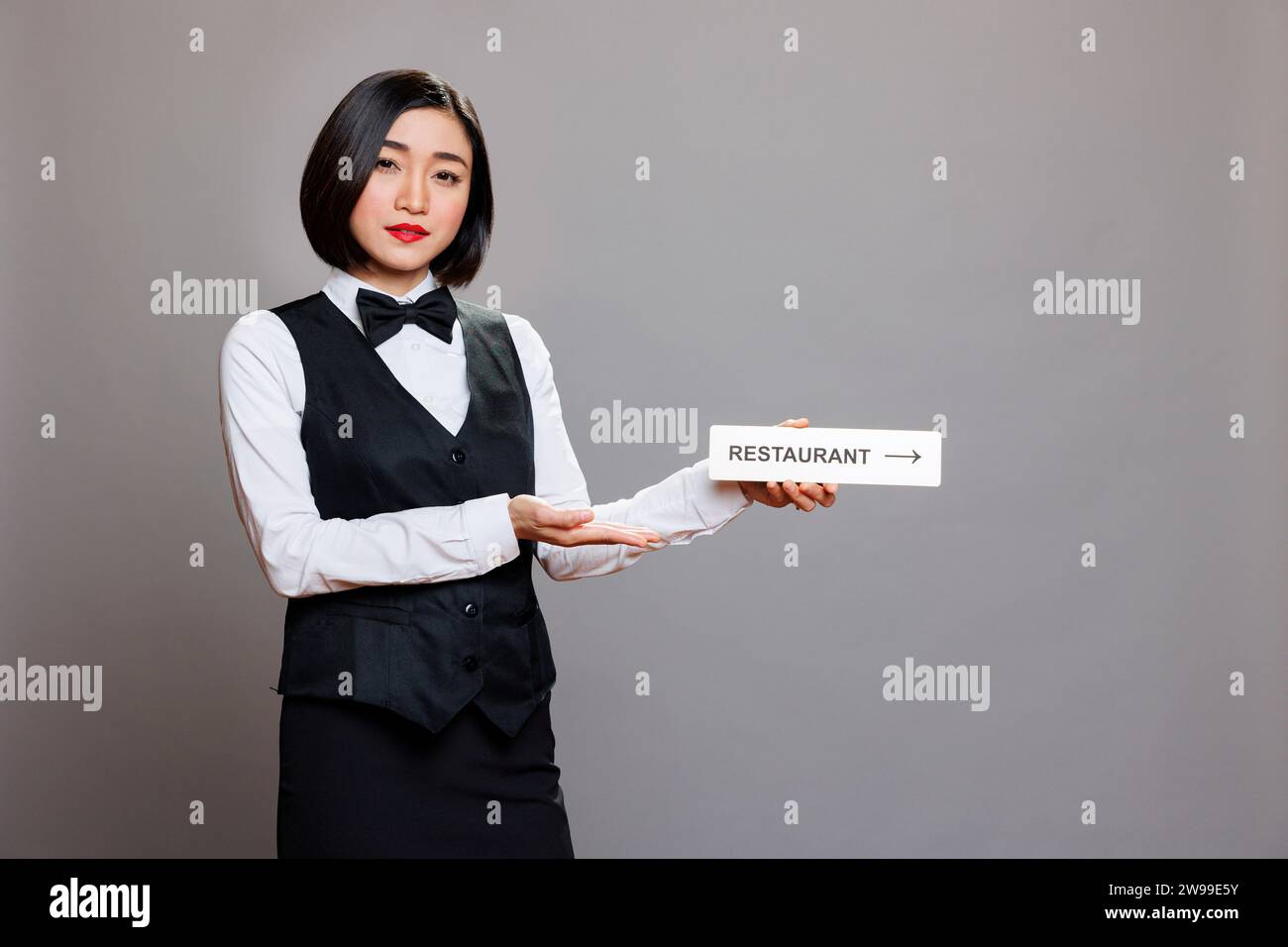 Asian waitress holding restaurant direction signage and looking at ...