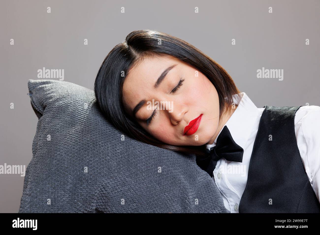 Exhausted sleepy asian waitress resting head on pillow, posing in ...