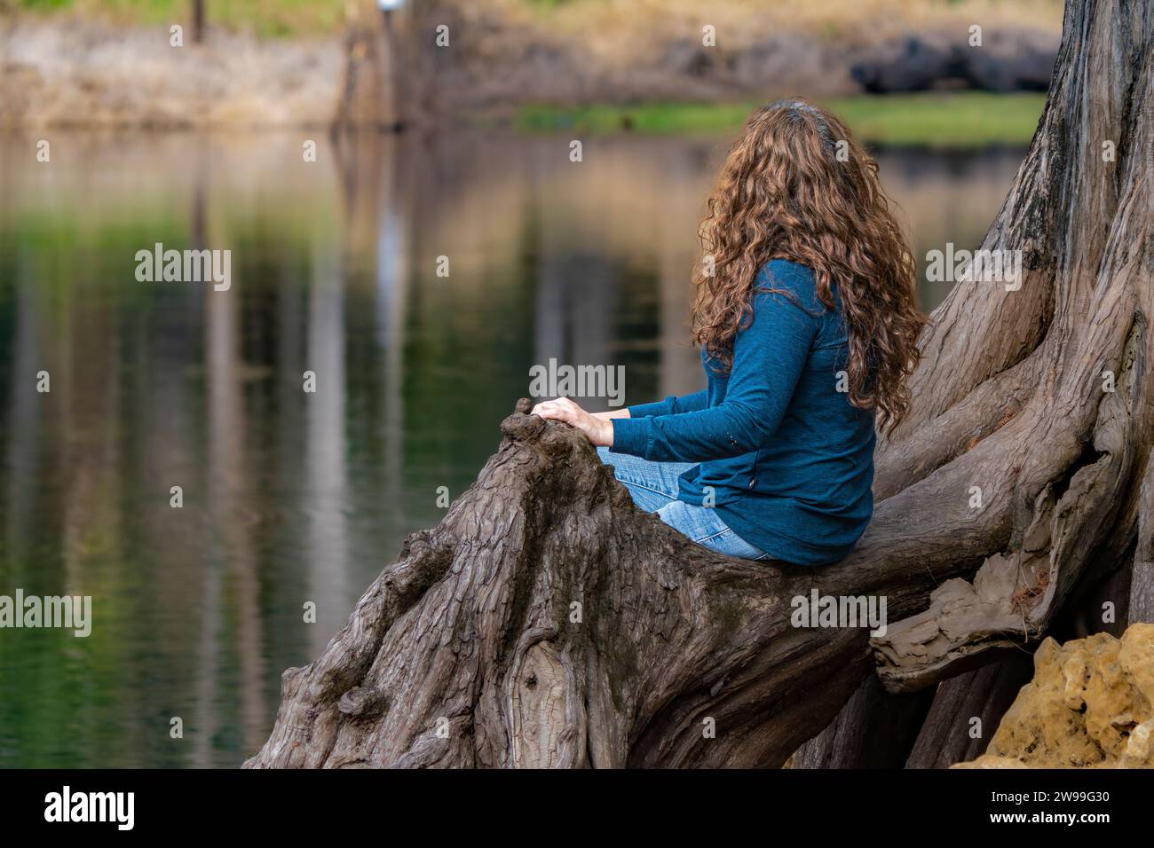 A Woman Is Seen Seated On The Side Of A Tree Trunk With A Serene