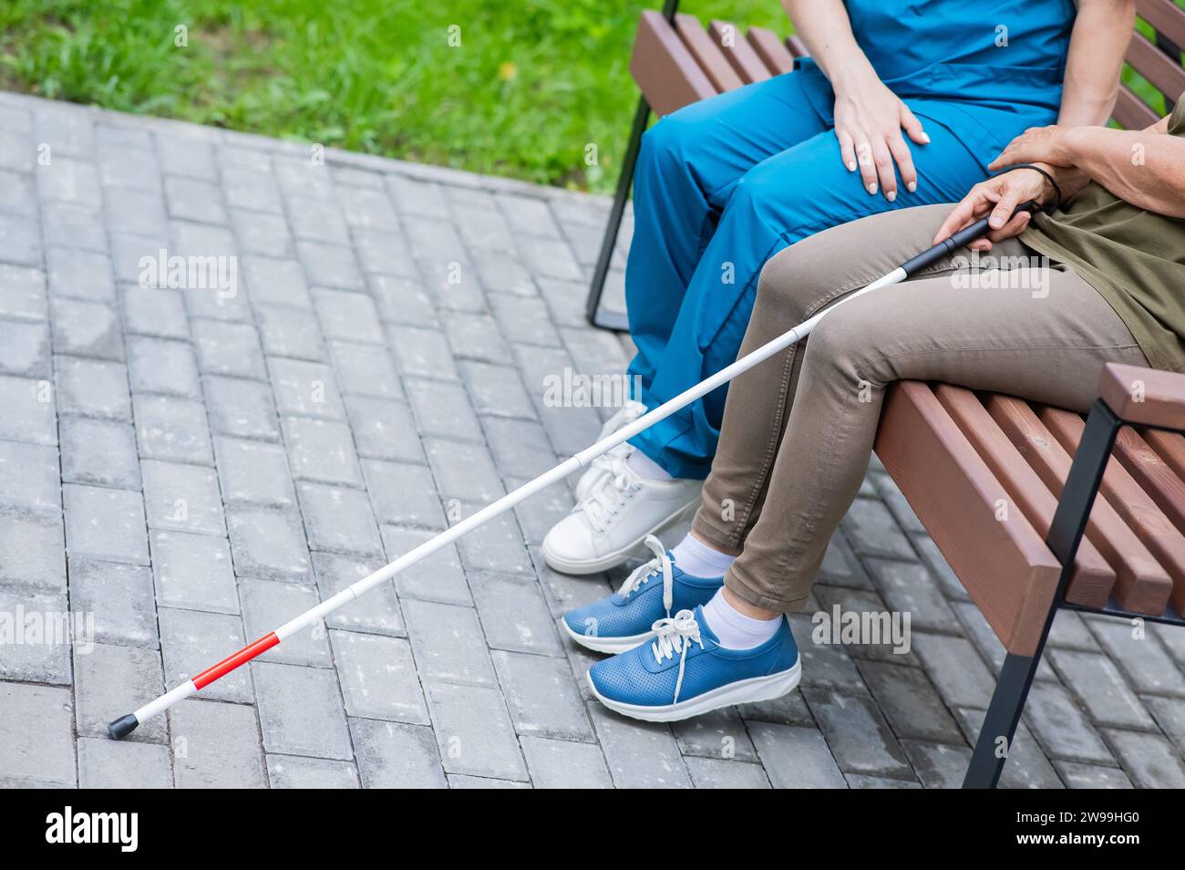 A nurse and an elderly blind woman are sitting on a bench in the park ...