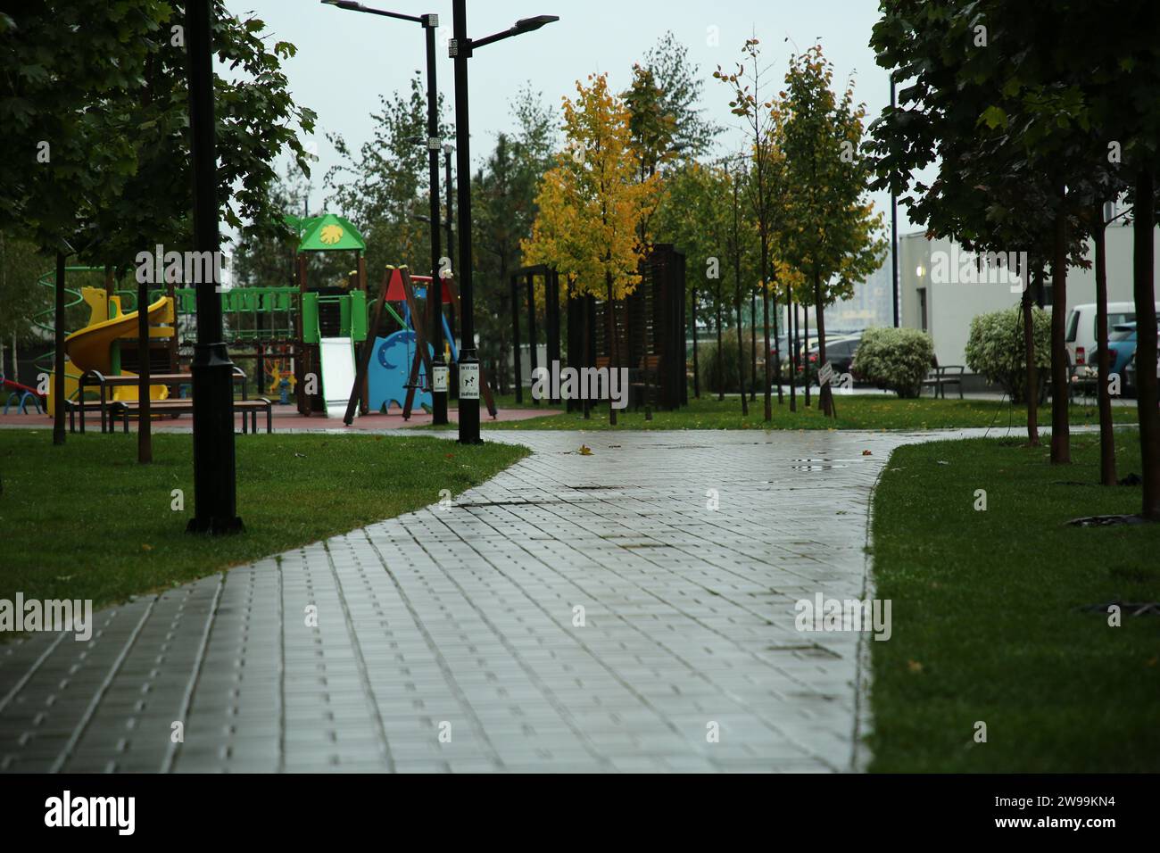 City street with colorful playground and puddles on pavement after rain ...