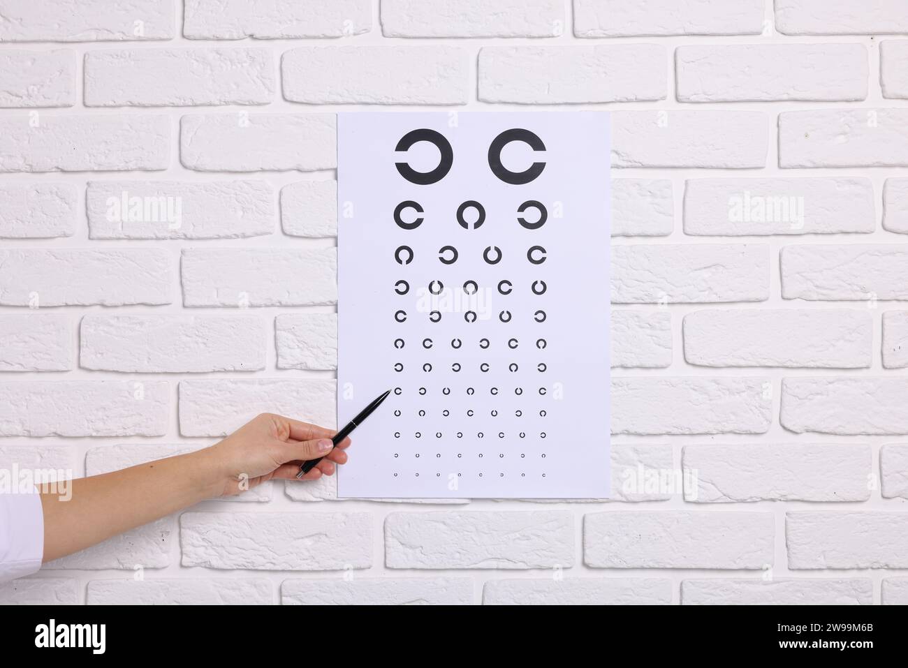 Ophthalmologist pointing at vision test chart on white brick wall ...