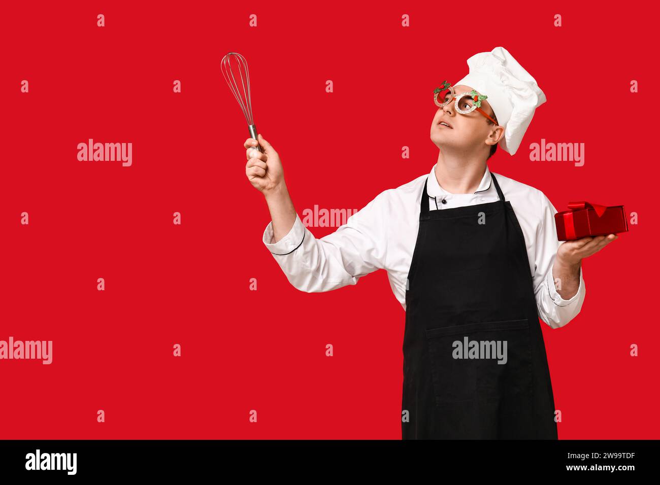 Portrait of young male chef in Christmas novelty glasses with whisk and ...