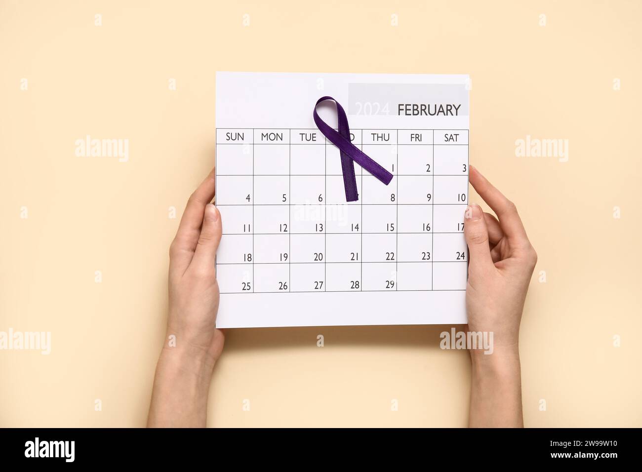 Female hands with purple ribbon and paper calendar on beige background ...